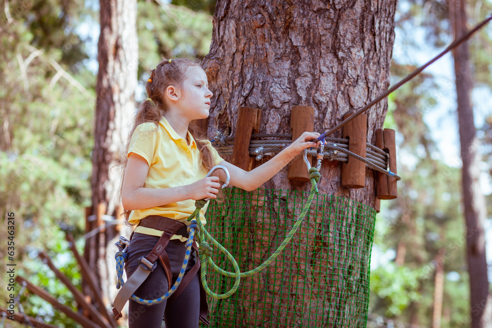 A child in a forest adventure park made of ropes. The girl is climbing ...