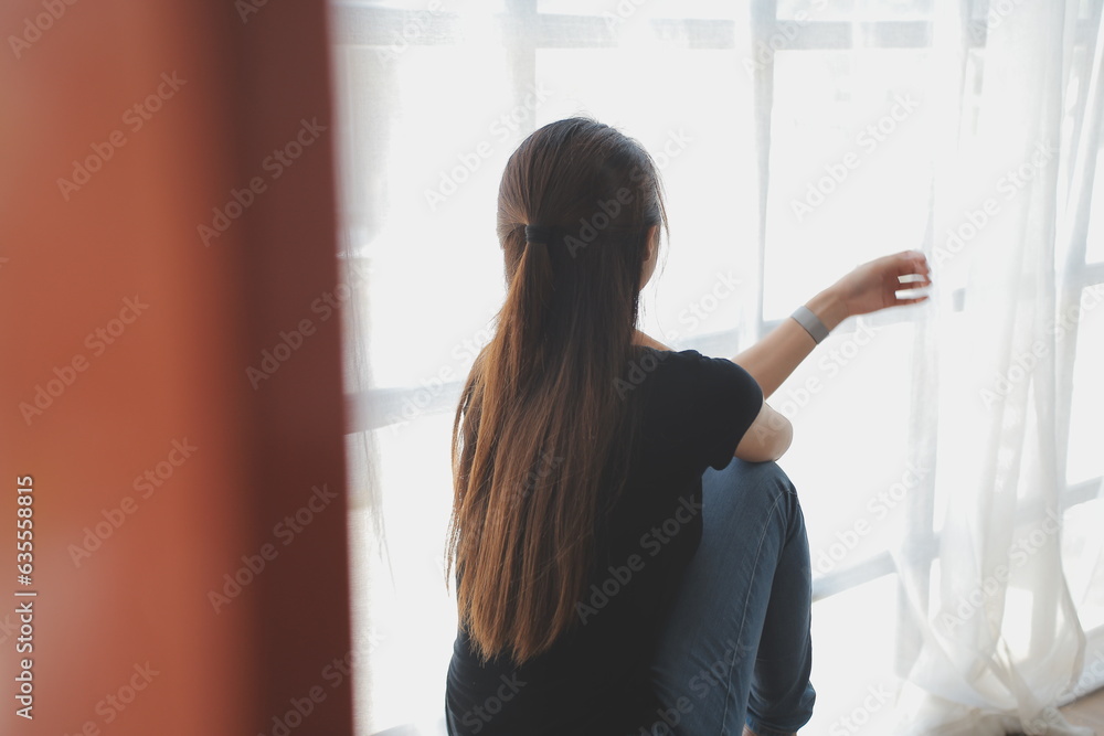 Thoughtful girl sitting on sill embracing knees looking at window, sad ...