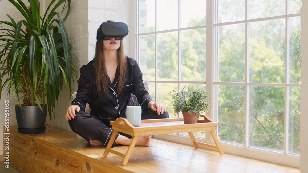 Beautiful young girl in a virtual reality headset. Drinking morning ...