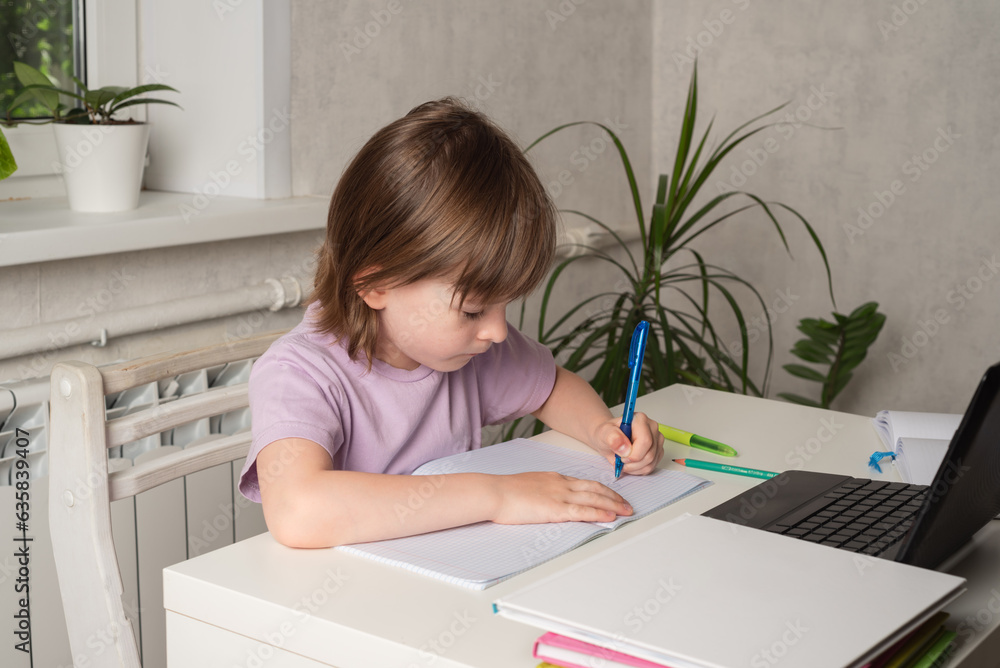 Happy girl sits at a table and works on a laptop and writes with her ...