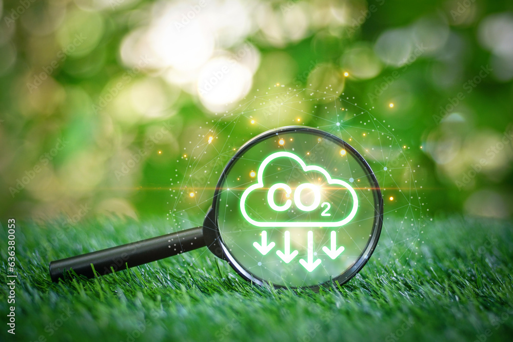 Magnifying glass focused on CO2 emission reduction icons on the grass in garden with green ...