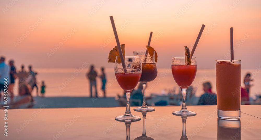 Bright cocktail drinks with blur beach party people and colorful sunset sea sky in background ...