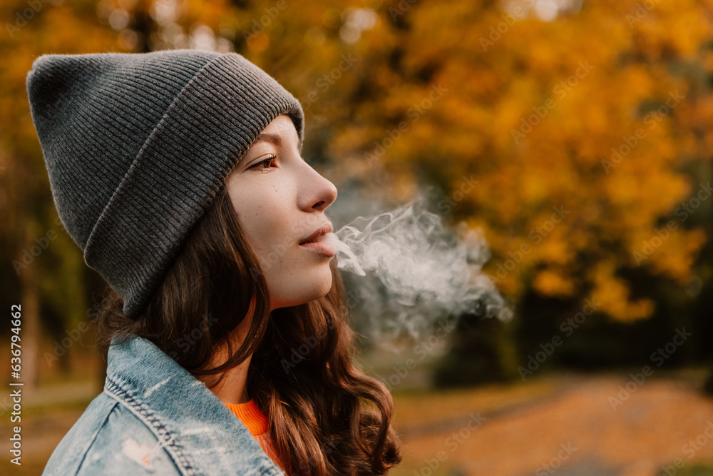 Young woman outside autumn park fall and smoking tobacco device ...