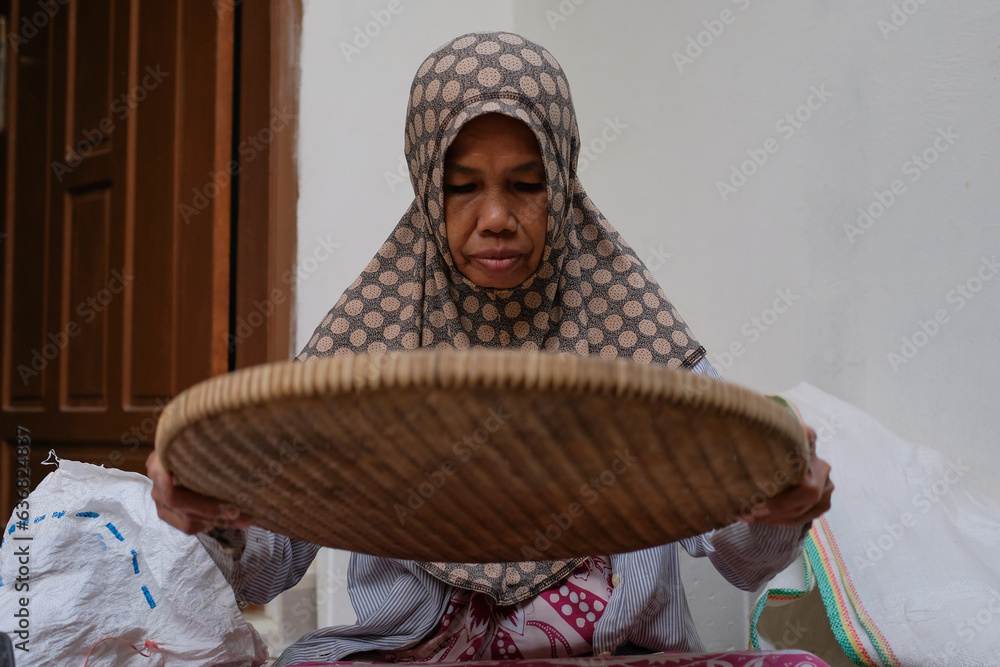 Asian old woman winnowing rice using a traditional basket to clean the ...