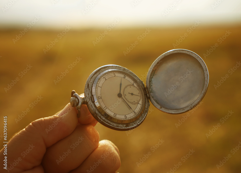 Man looking at traditional opened pocket watch, shot on sunset meadow ...