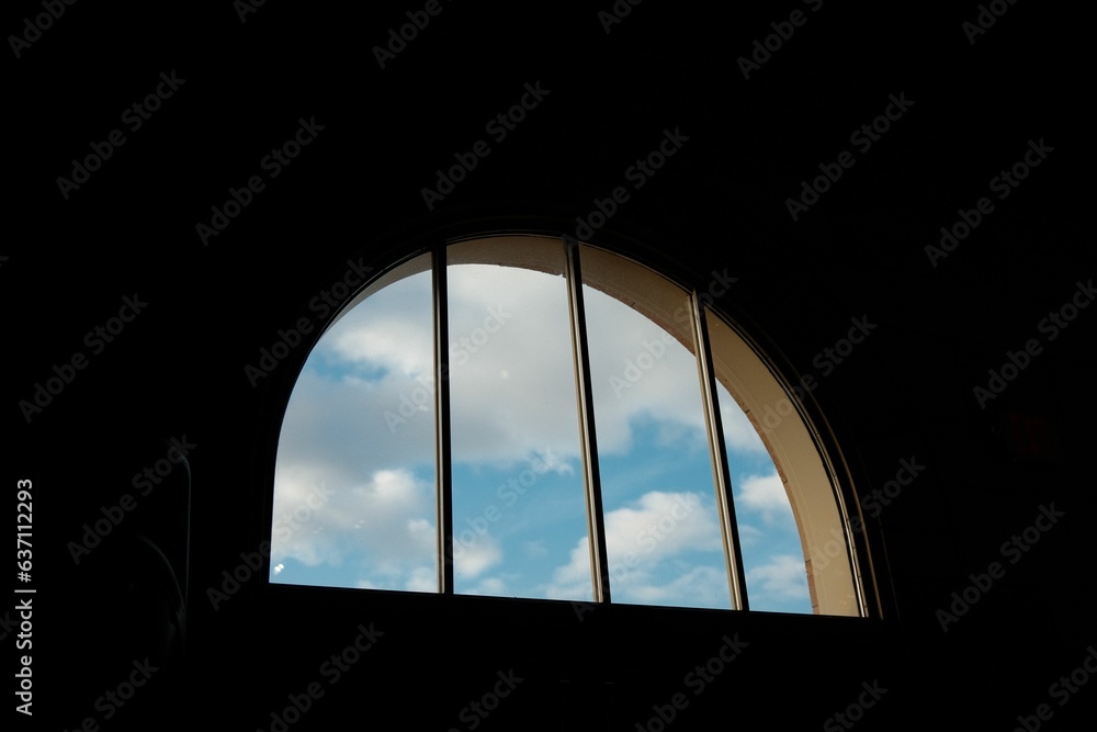 Clouds in the blue sky seen from a semi-circular, arched window with ...
