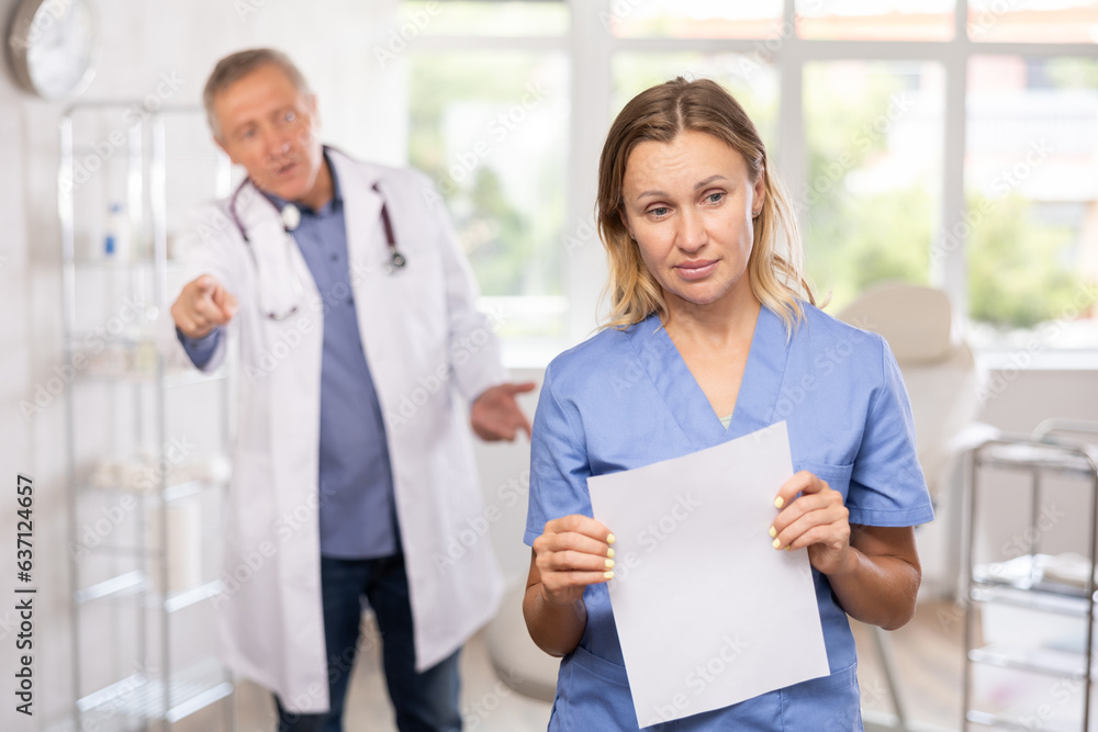 Frustrated female doctor standing in medical office with papers in ...