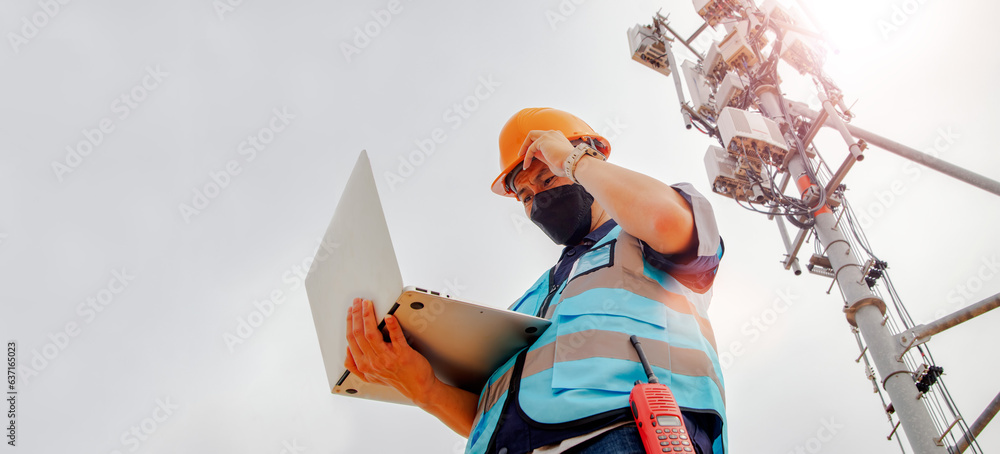 Helmeted asian male engineer works field with telecommunication tower ...