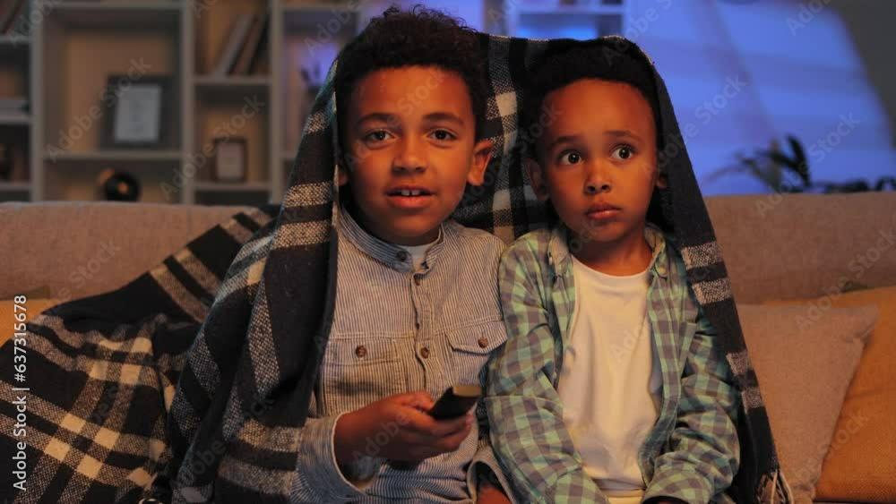Two little African American brothers are sitting on the sofa covered ...