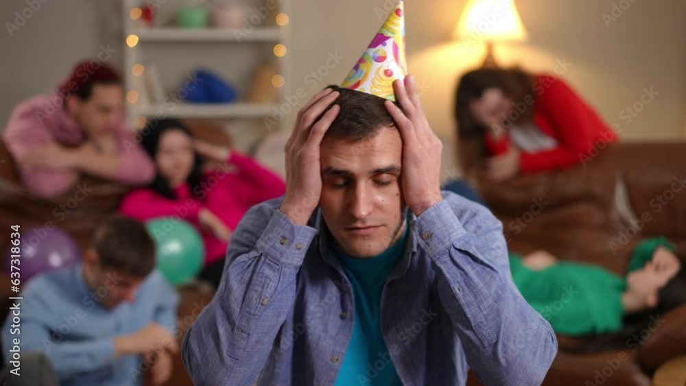Exhausted young man in party hat holding head in hands and looking at ...