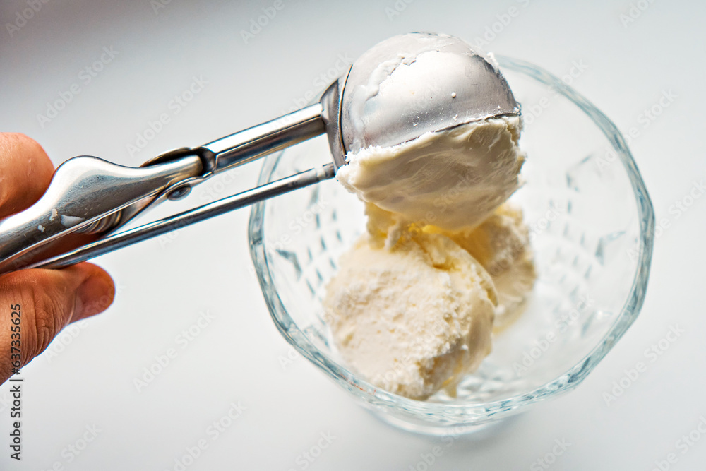 A human hand puts a scoop of ice cream into a glass bowl with a scoop ...