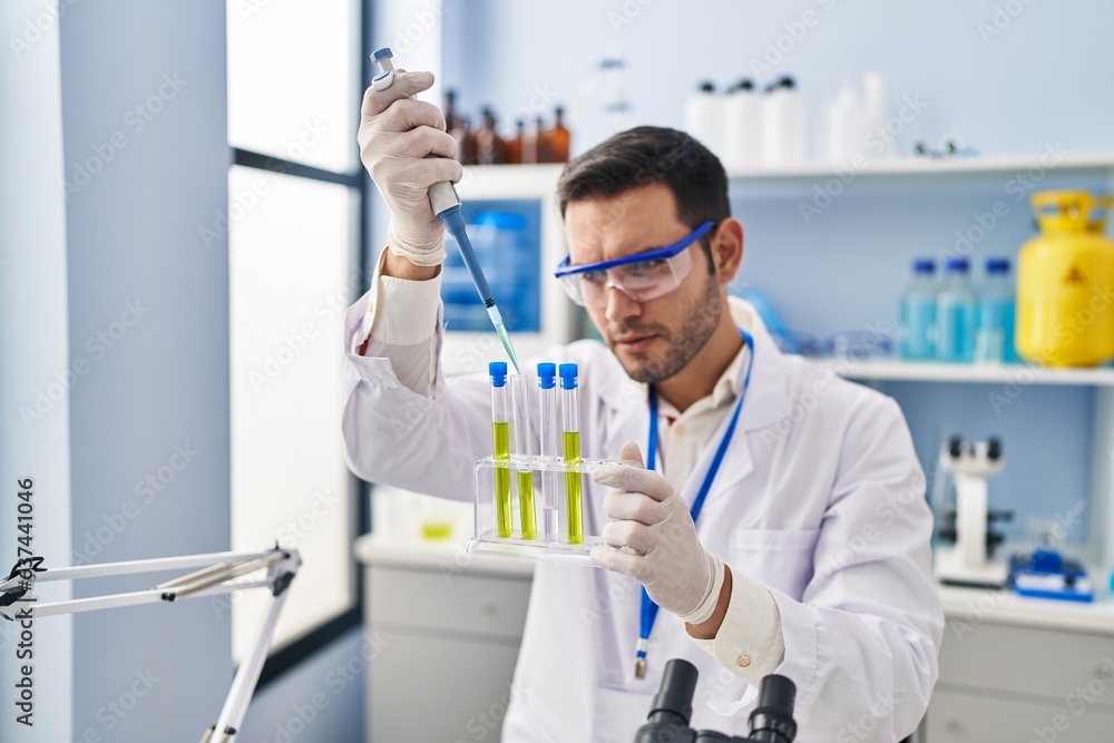 Young hispanic man scientist measuring liquid using pipette at ...