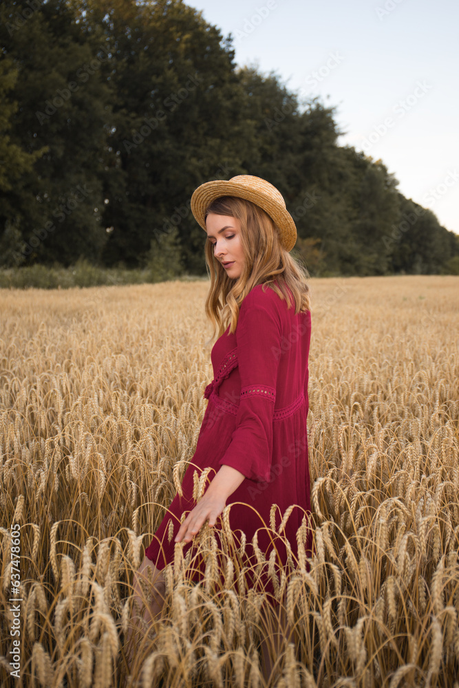 Blonde woman walking across wheap field. Lady wearing straw hat and ...