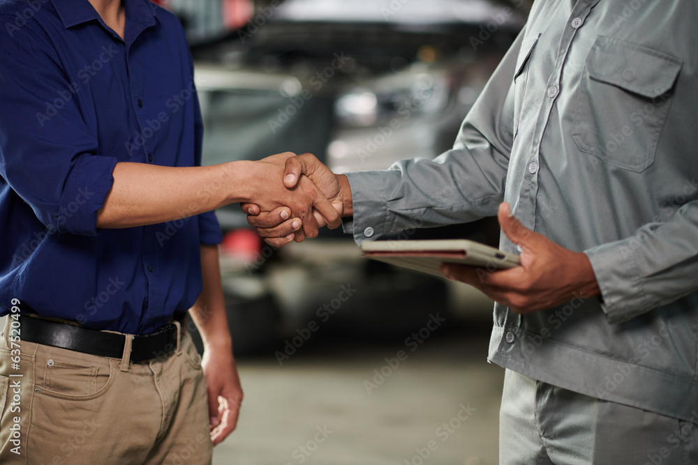 Mechanic and car owner shaking hands and signing document Stock Photo ...