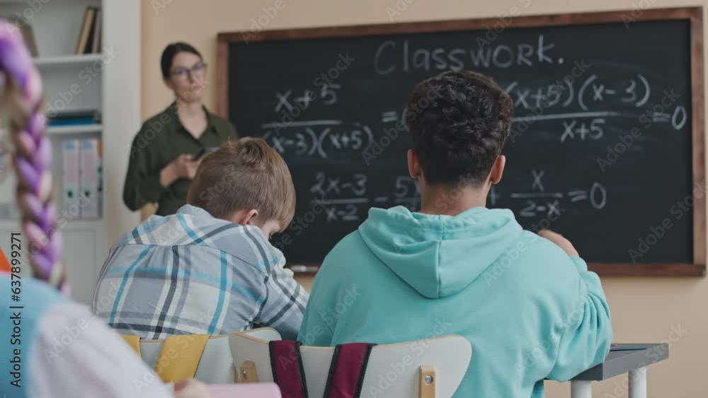 Back view of schoolboy raising his hand to solve Math equation ...