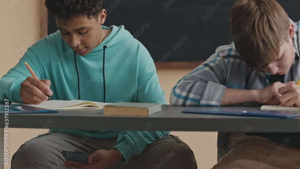 Medium shot of Biracial preteen schoolboy using smartphone hidden under ...