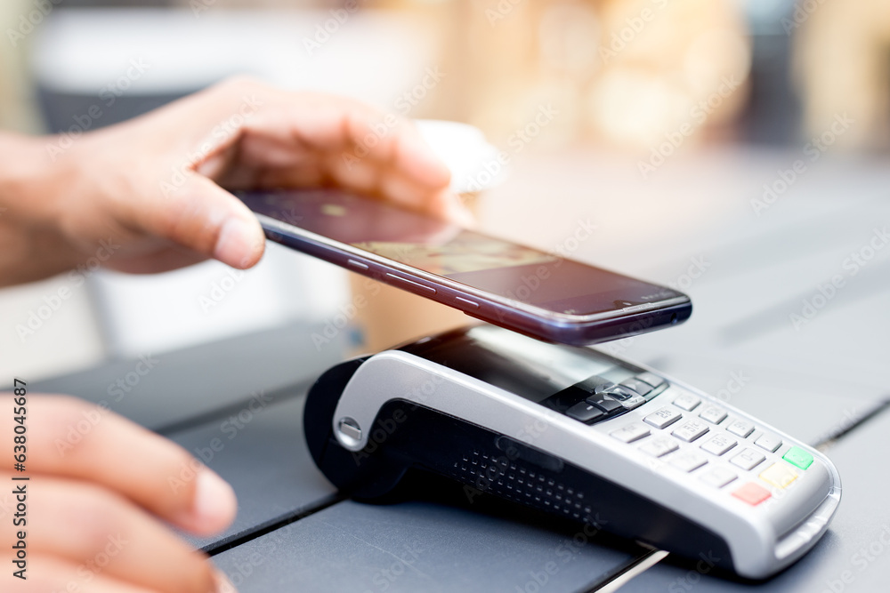 Hands using an NFC mobile phone to make a contactless payment in a ...