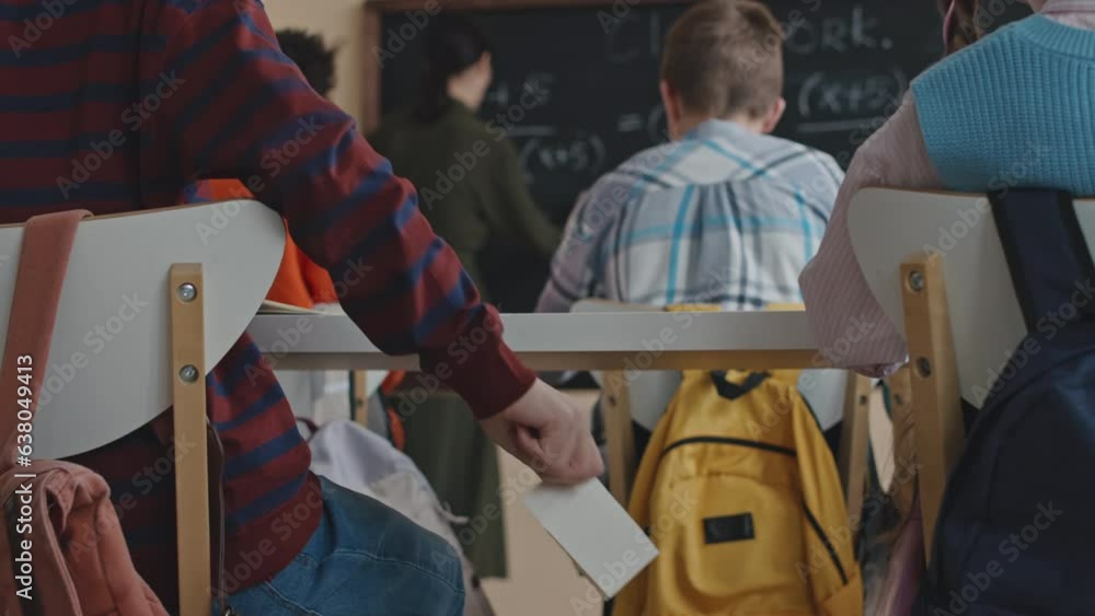 Back view of schoolboy passing cheat sheet to his classmate while ...