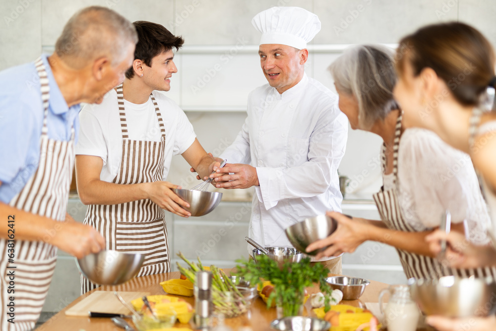 Adult male chef at master class teaches group of people how to cook ...