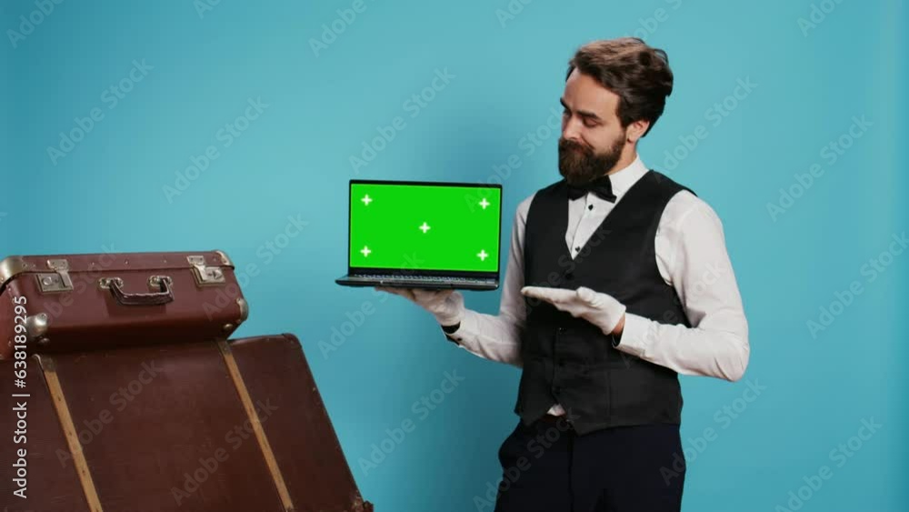 Classy bellhop presents greenscreen on laptop display in studio while ...