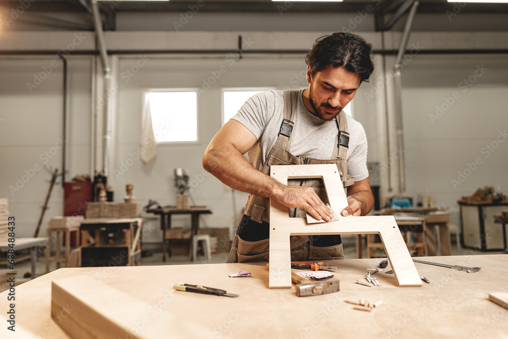 Young man carpenter wearing uniform working in joinery making wooden ...