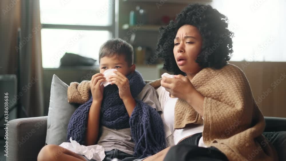 Sick cute family sitting on sofa under the warm blanket coughing sneezing and having severe ...