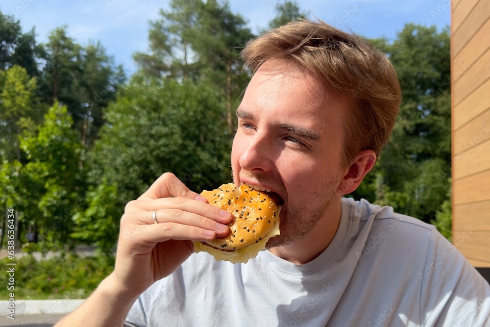 Portrait of young happy man is eating, biting juicy delicious burger ...