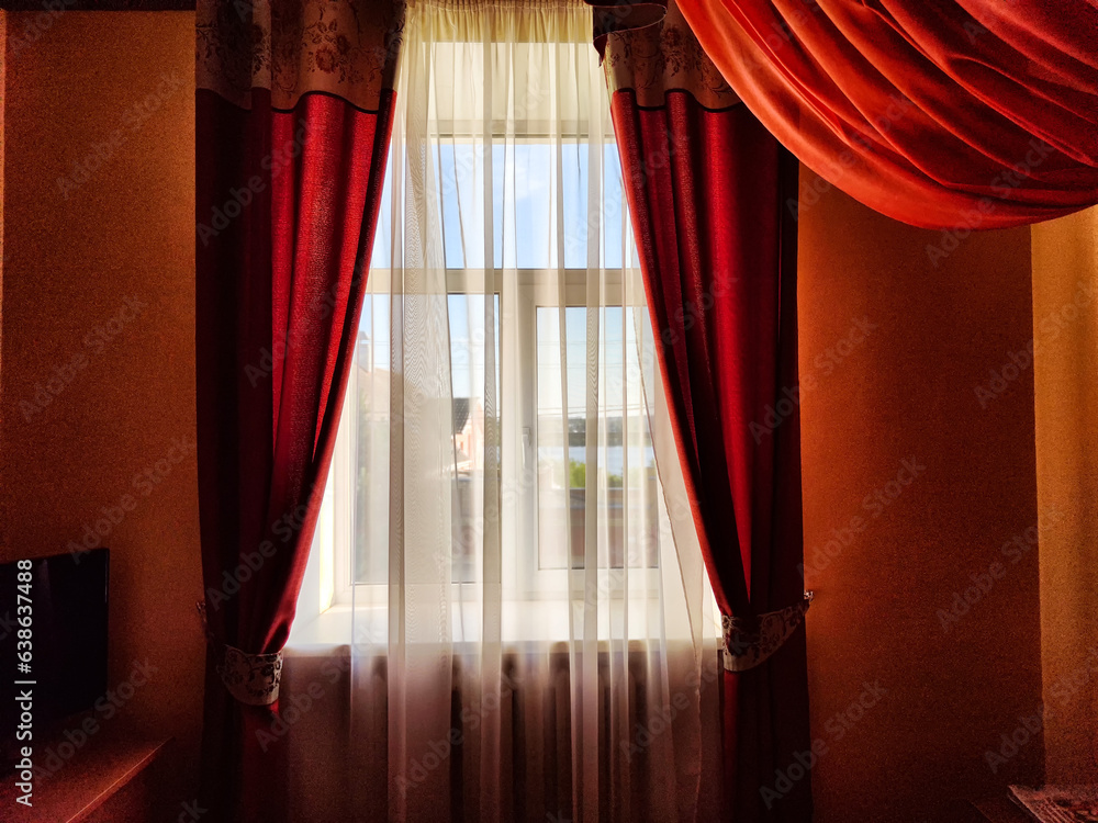Beautiful red curtains on the window and transparent tulle fabric ...