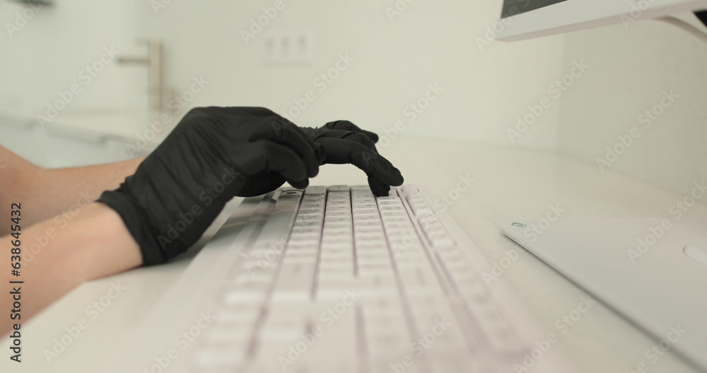 Hands in black nitrile gloves using keyboard while doing work in clinic ...
