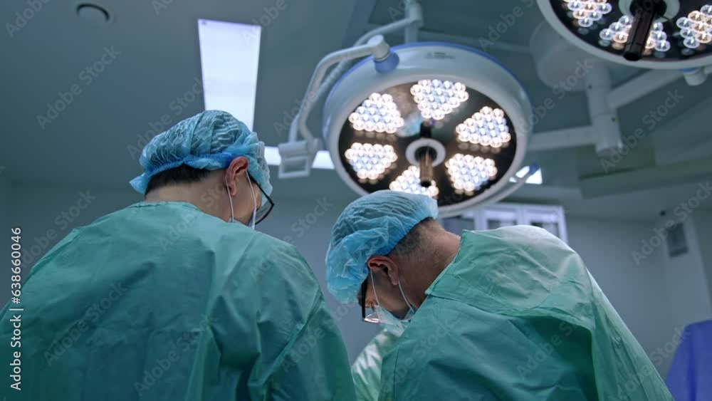 Rear view of two male doctors working at operational table. Uniformed ...