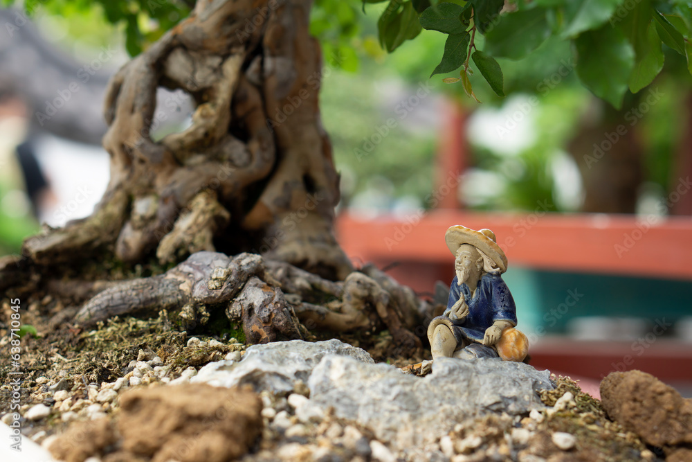 Tiny sculpture under the bonsai miniature. Evergreen tree in a tray ...