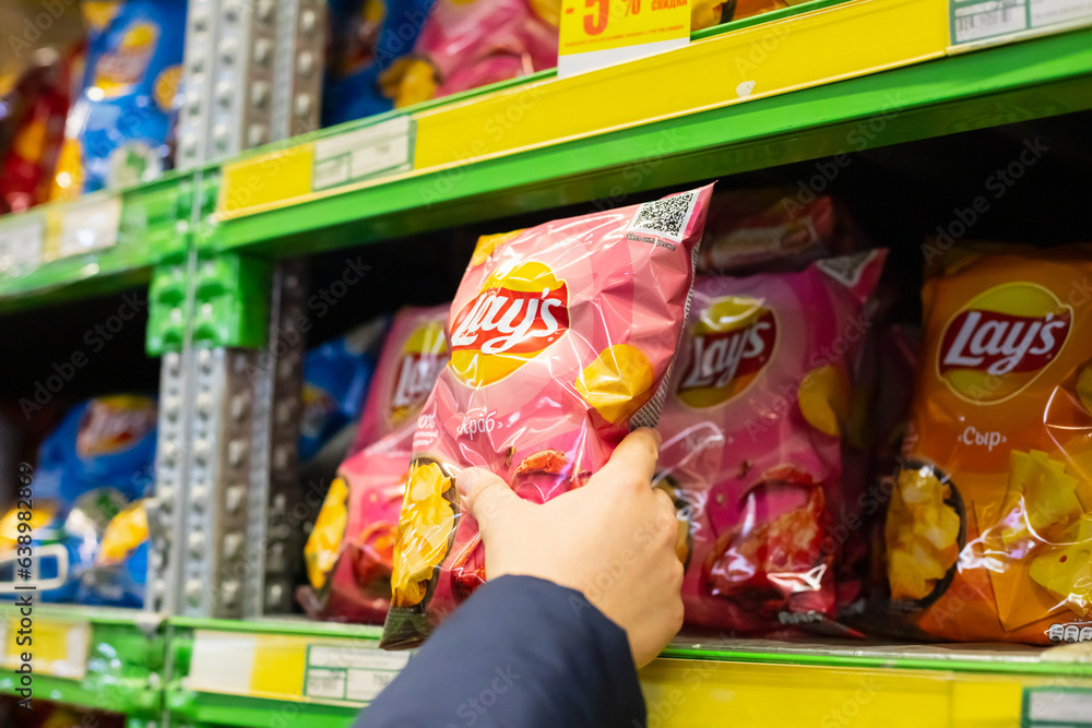 Lays potato chips packaging on store shelf. Man's male hand takes ...