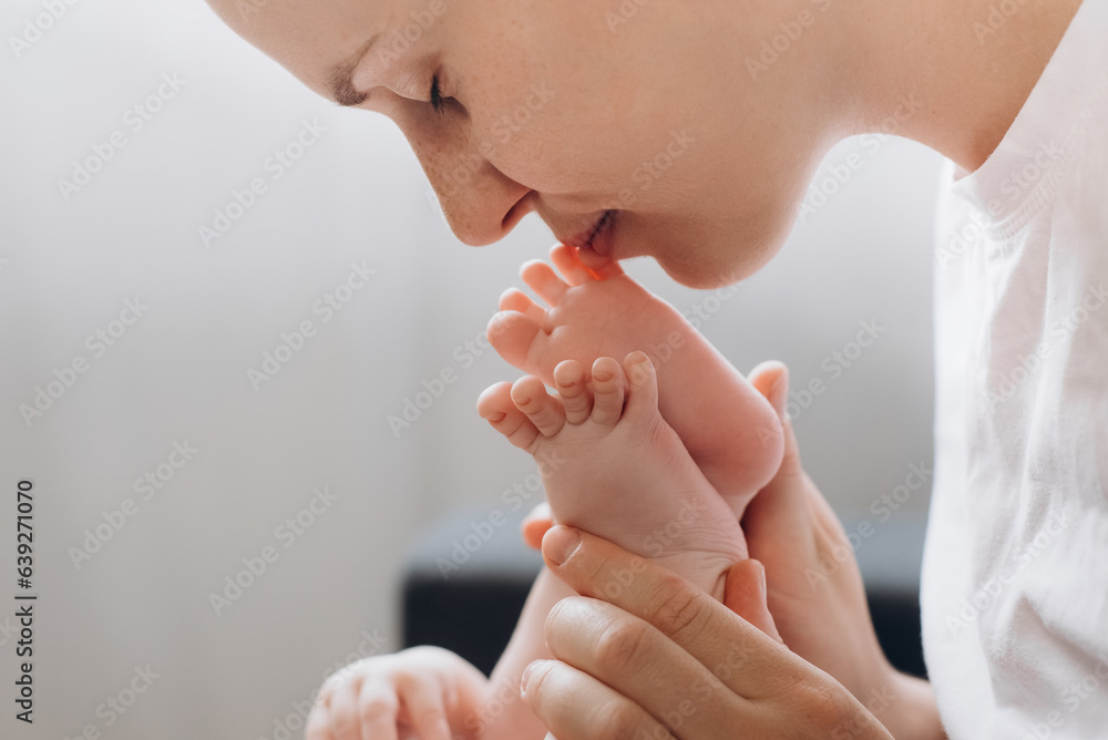 Close up of happy young loving mommy gently kiss little feet sitting on ...