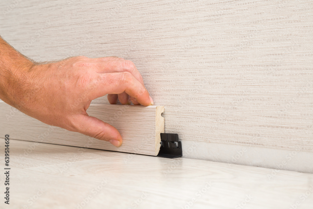 Young adult man hand installing new beige baseboard on wall and ...