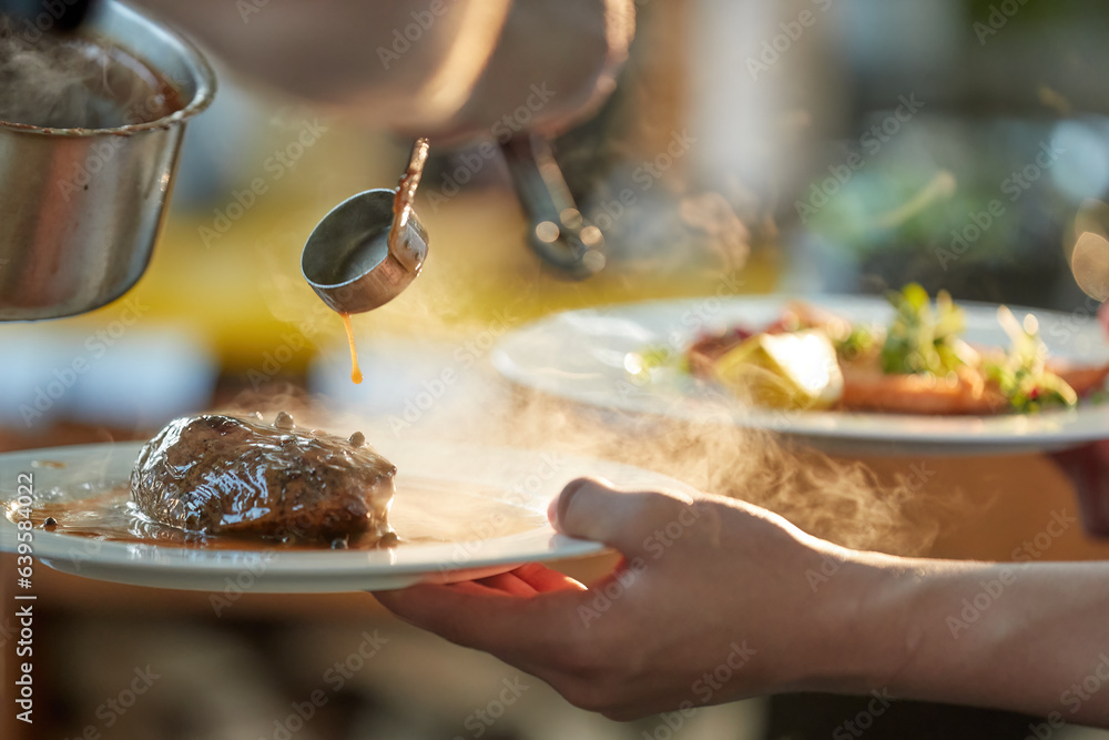 Chef pouring sauce over steak. Close up of cooking at garden party. Two ...