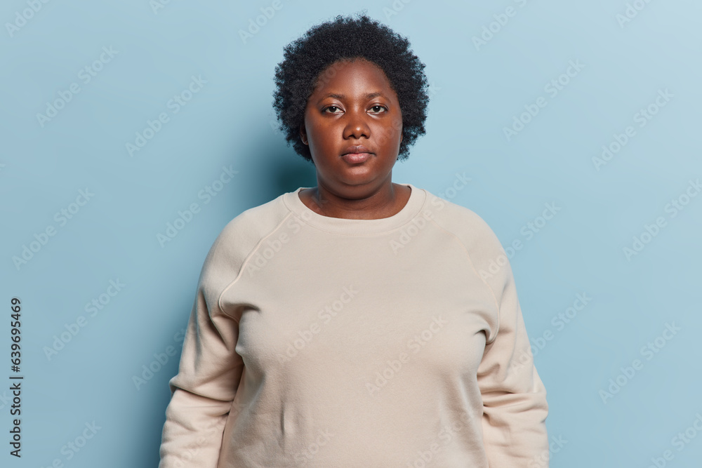 Portrait of serious dark skinned overweight young woman looks directly ...