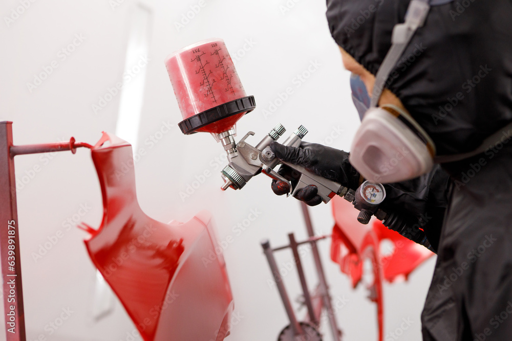 Auto painter spraying a car body with red paint and protective gear ...