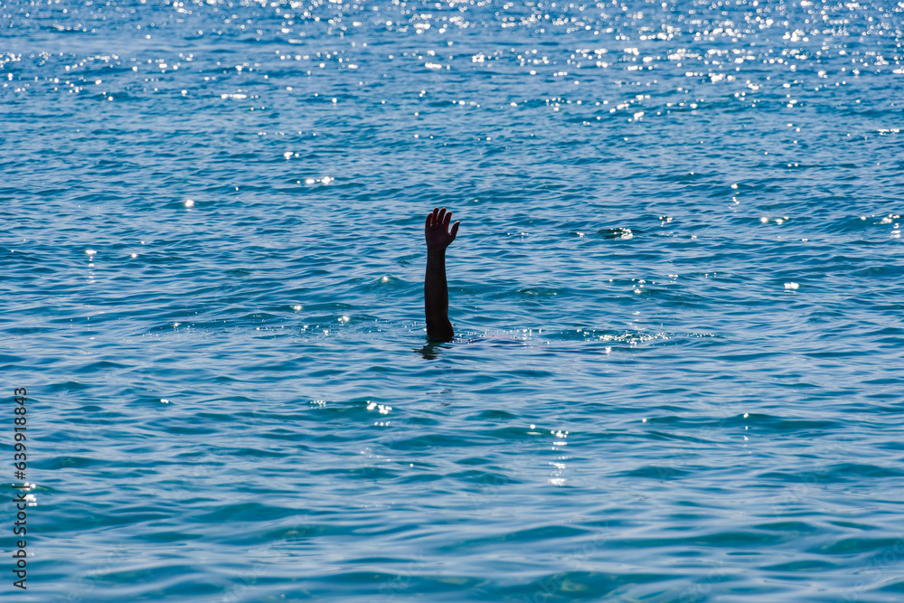 Drowning man concept, with a male raised hand with an open palm visible ...