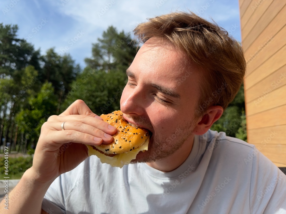 Portrait of young happy man is eating, biting juicy delicious burger ...