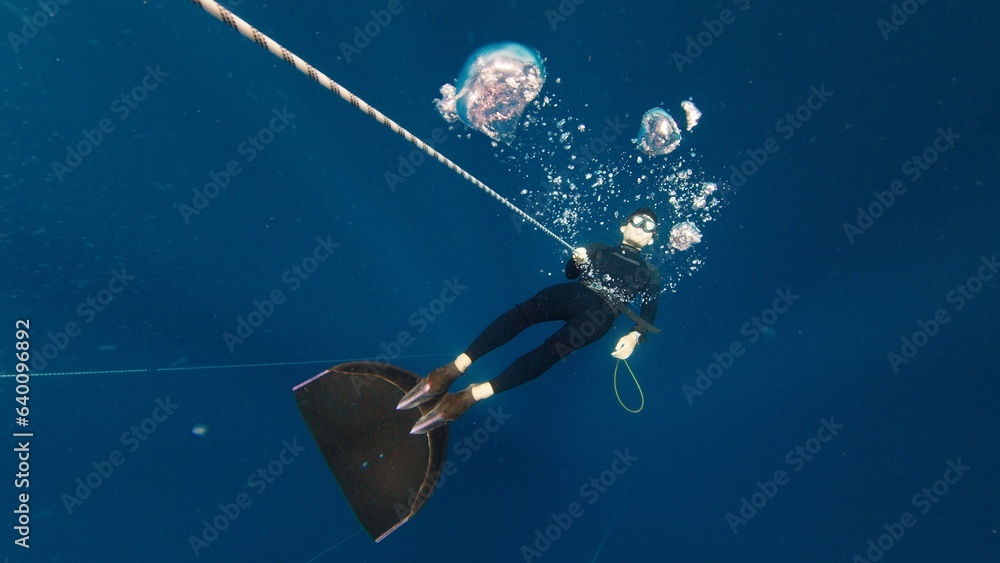Freediving on the rope in a sea. Male freediver makes bubbles ...