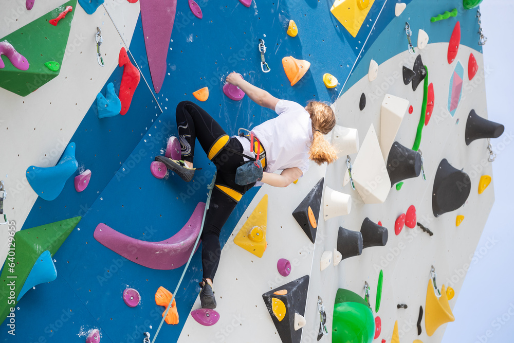 The climber climbs the artificial stone wall with the help of safety ...