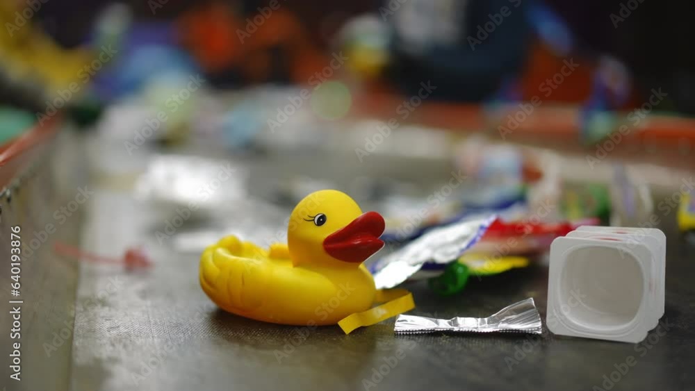 Close-up yellow rubber duck on conveyor belt with garbage and blurred ...
