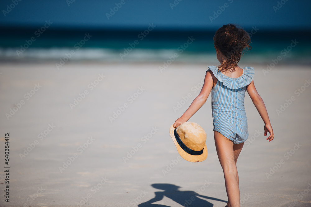 Rear view of a beautiful little girl walking on the beach in a swimsuit ...
