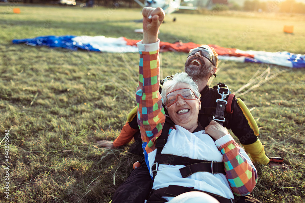 Senior woman skydiving with her instructor and landing on a field with ...