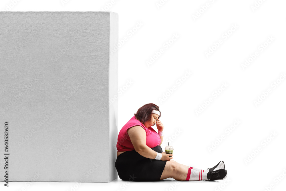 Sad overweight woman in sportswear holding a healthy green shake and ...