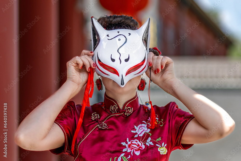 A young Asian girl walks in national clothes with a white mask in the ...