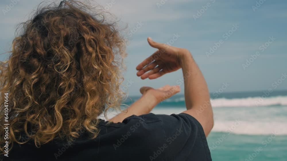 Anonymous man with long curly hair stay on ocean beach moving hands as ...