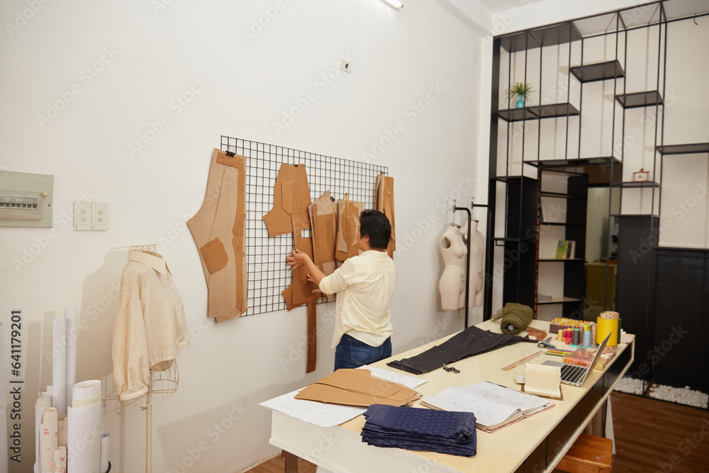 Back view of creative female tailor taking sketches from tailoring desk ...