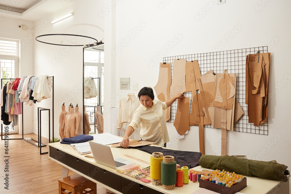 Back view of creative female tailor taking sketches from tailoring desk ...