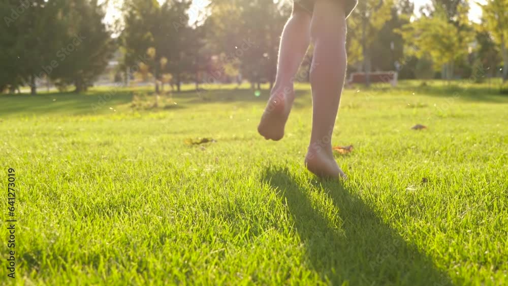 Kids legs are running close-up on the green grass. A boy runs with his ...